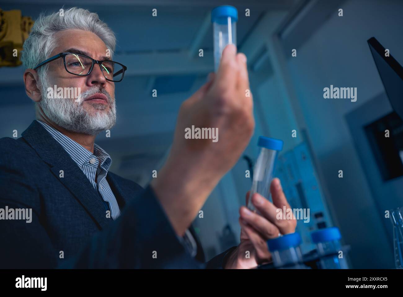 Scientist in the laboratory holding test tube and intently looking at ...