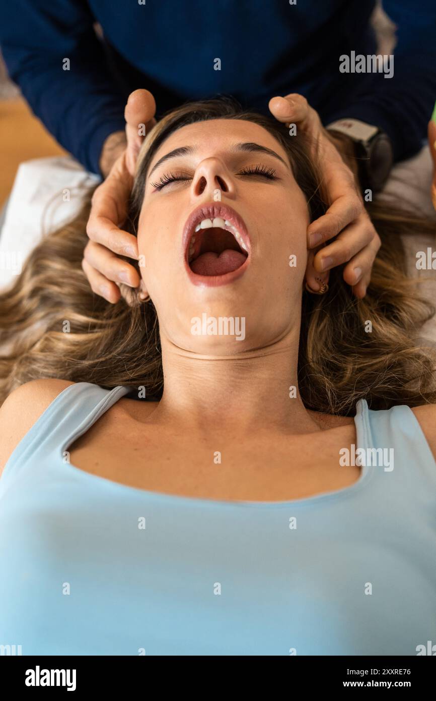 Close-up of a young woman receiving osteopathic treatment for temporomandibular joint (TMJ ...