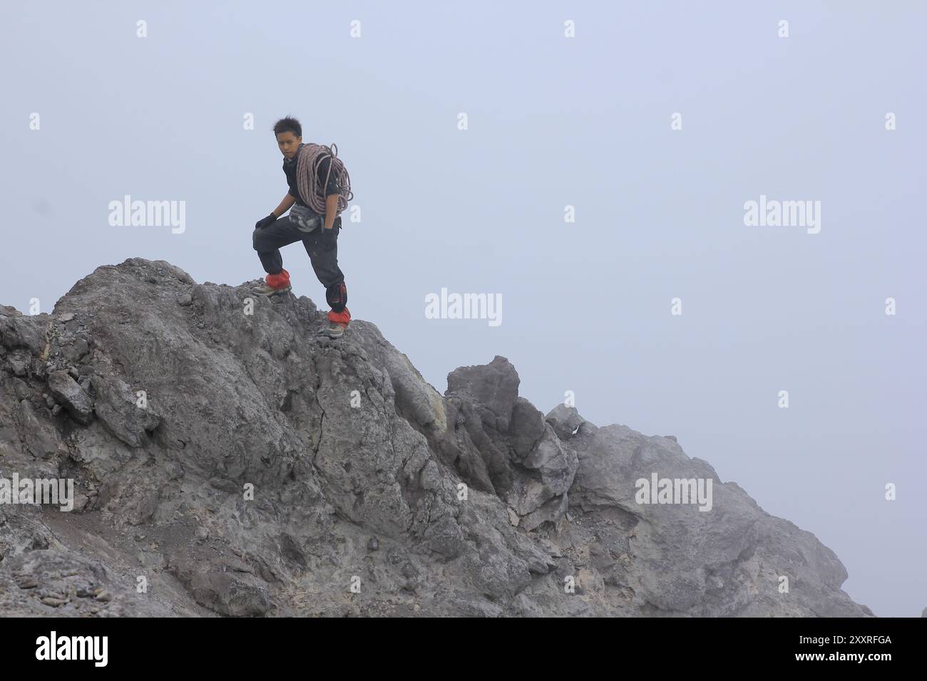A climber stands on volcanic rock which is the highest point of the ...