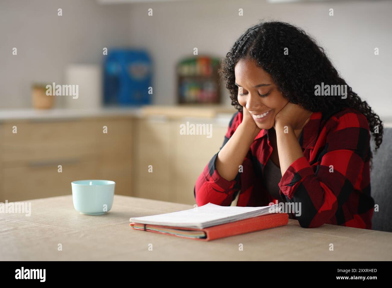 Happy black student studying and learning reading notes in the kitchen ...