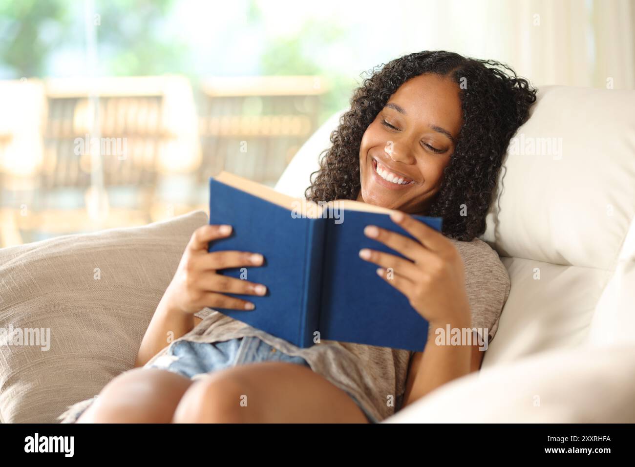 Happy black woman reading a paper book sitting in a sofa at home Stock ...