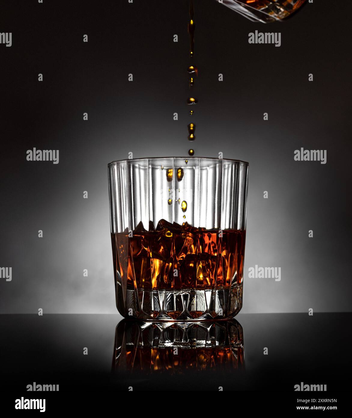 Pouring whisky into a crystal glass with ice cubes, circular gradation ...