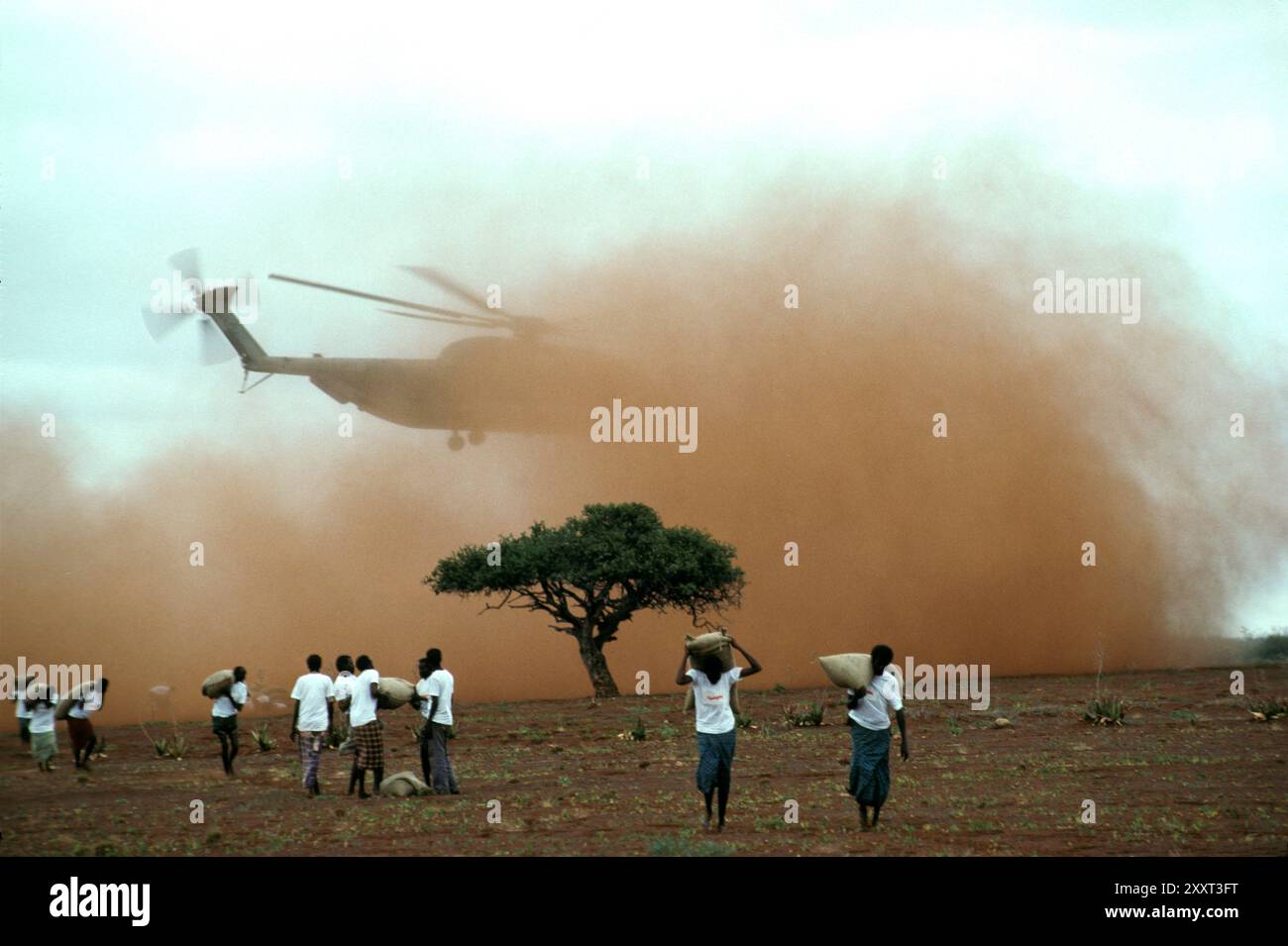 Men carry sacks of grain delivered by a helicopter to a food ...