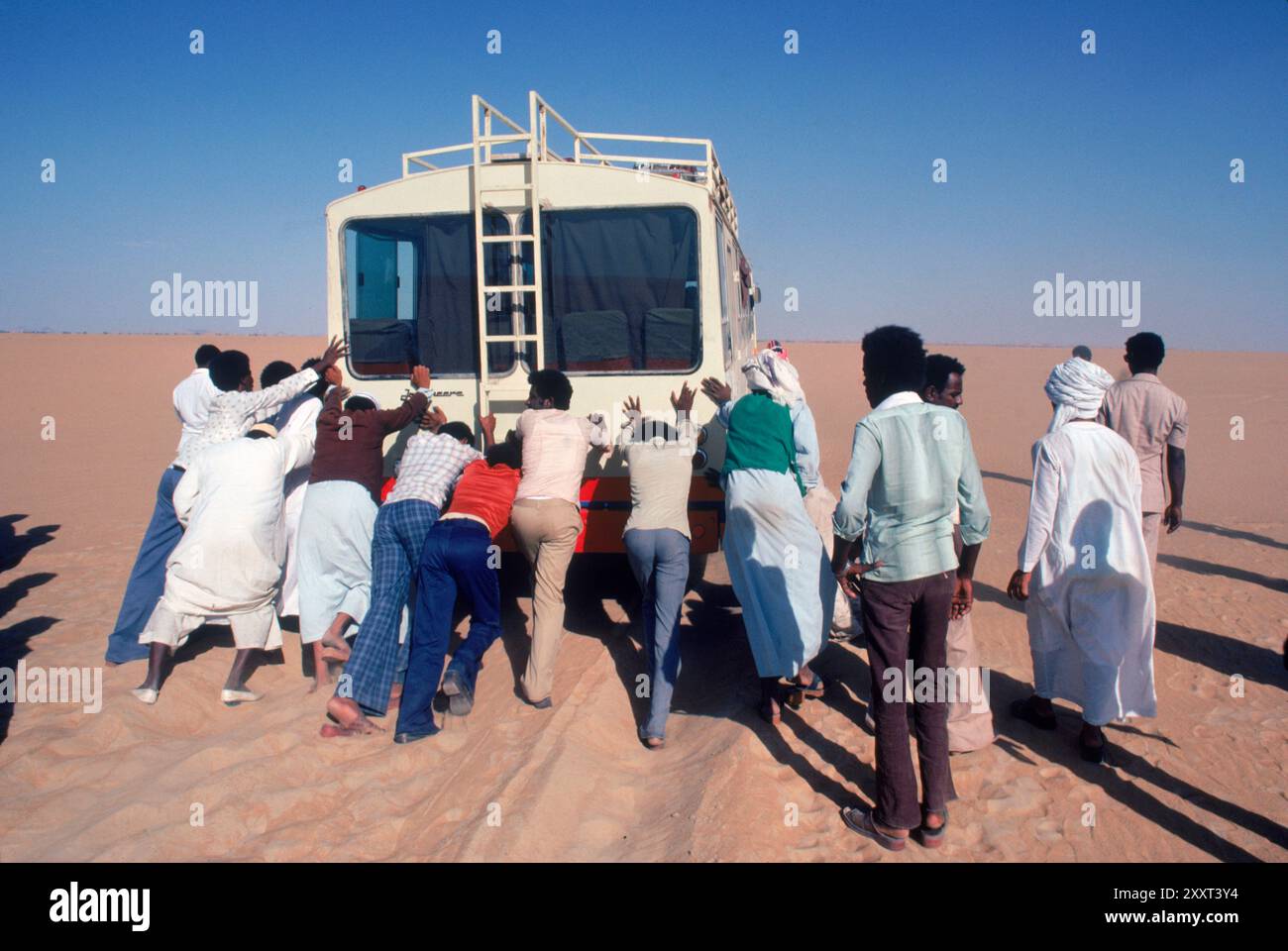 Passengers push a bus that has gotten stuck in the sand in the desert ...