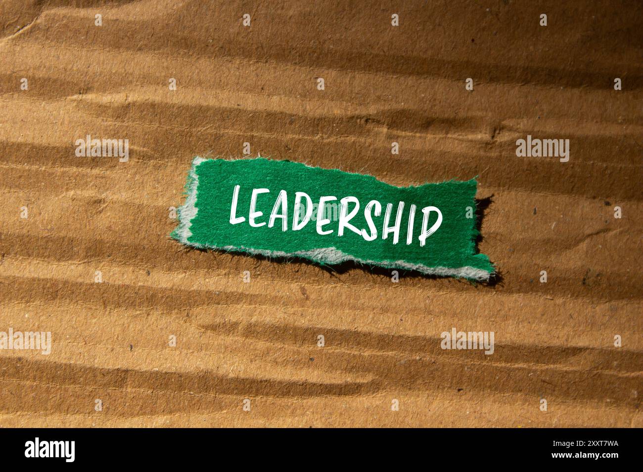 Leadership message written on ripped torn green paper piece with cardboard background ...