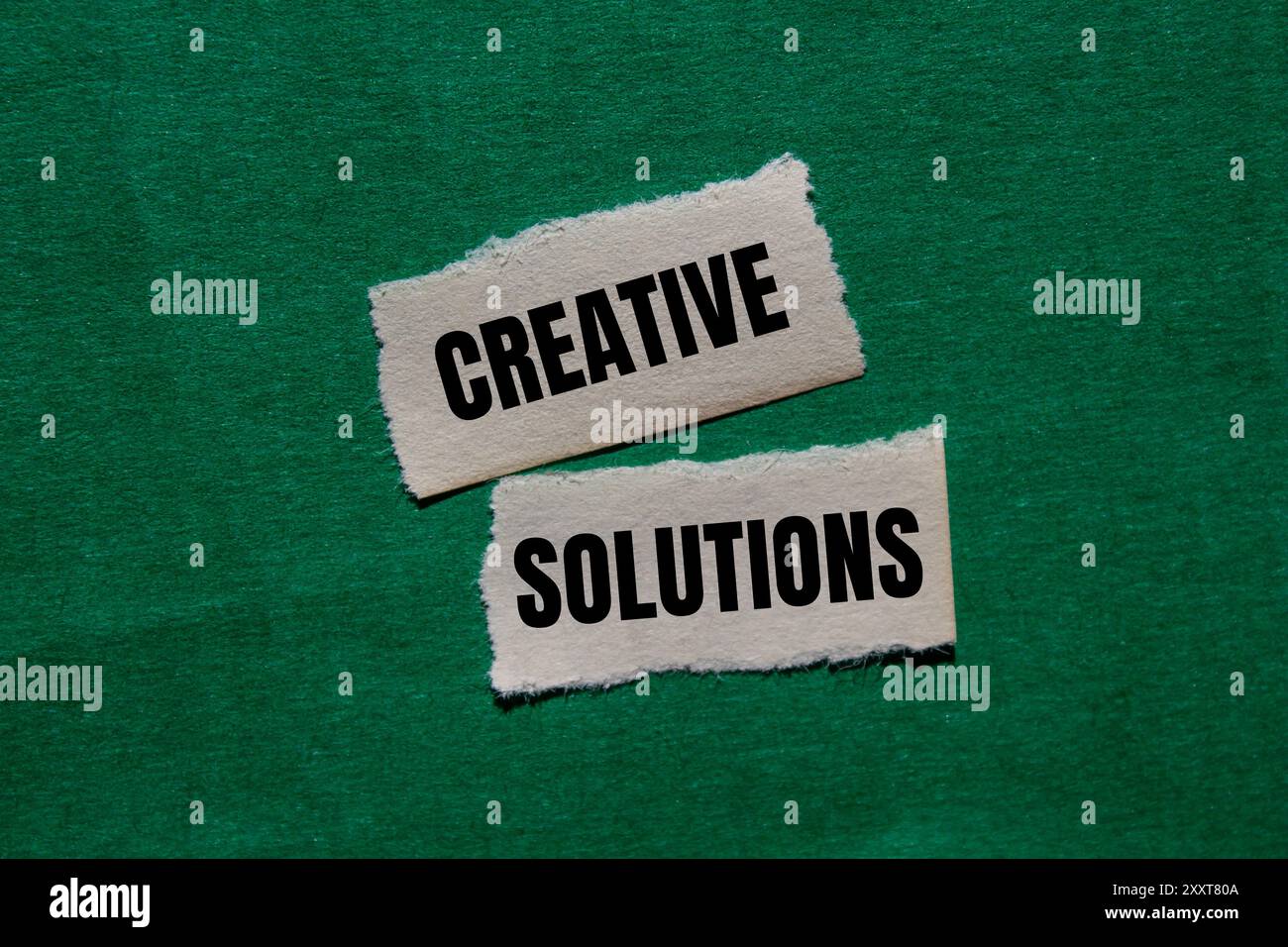 Creative solutions message written on ripped torn paper pieces with green background. Conceptual ...