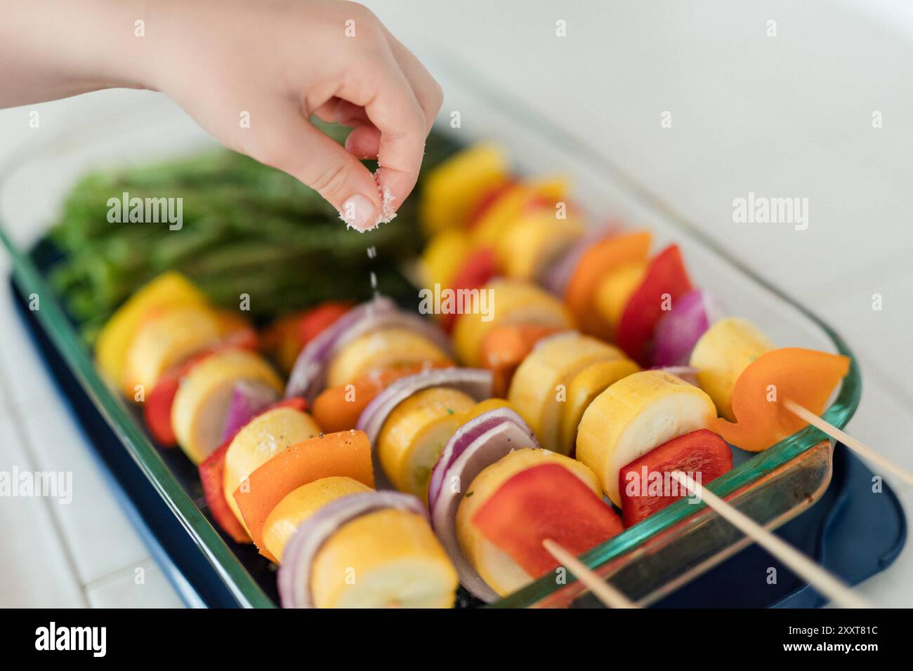 Hand sprinkling salt on vegetable skewers in a glass dish Stock Photo ...