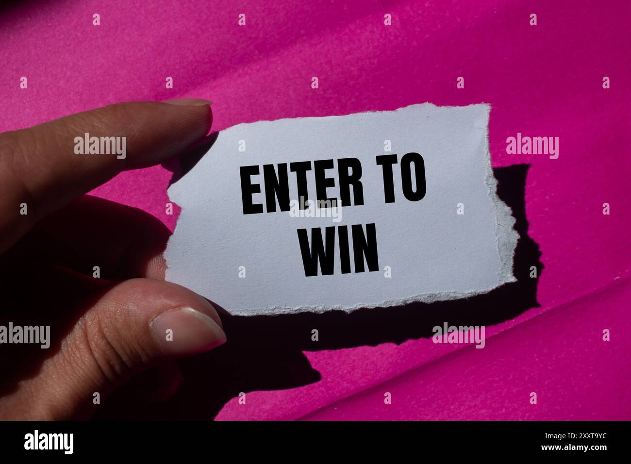 Enter to win message written on ripped paper piece with pink background ...