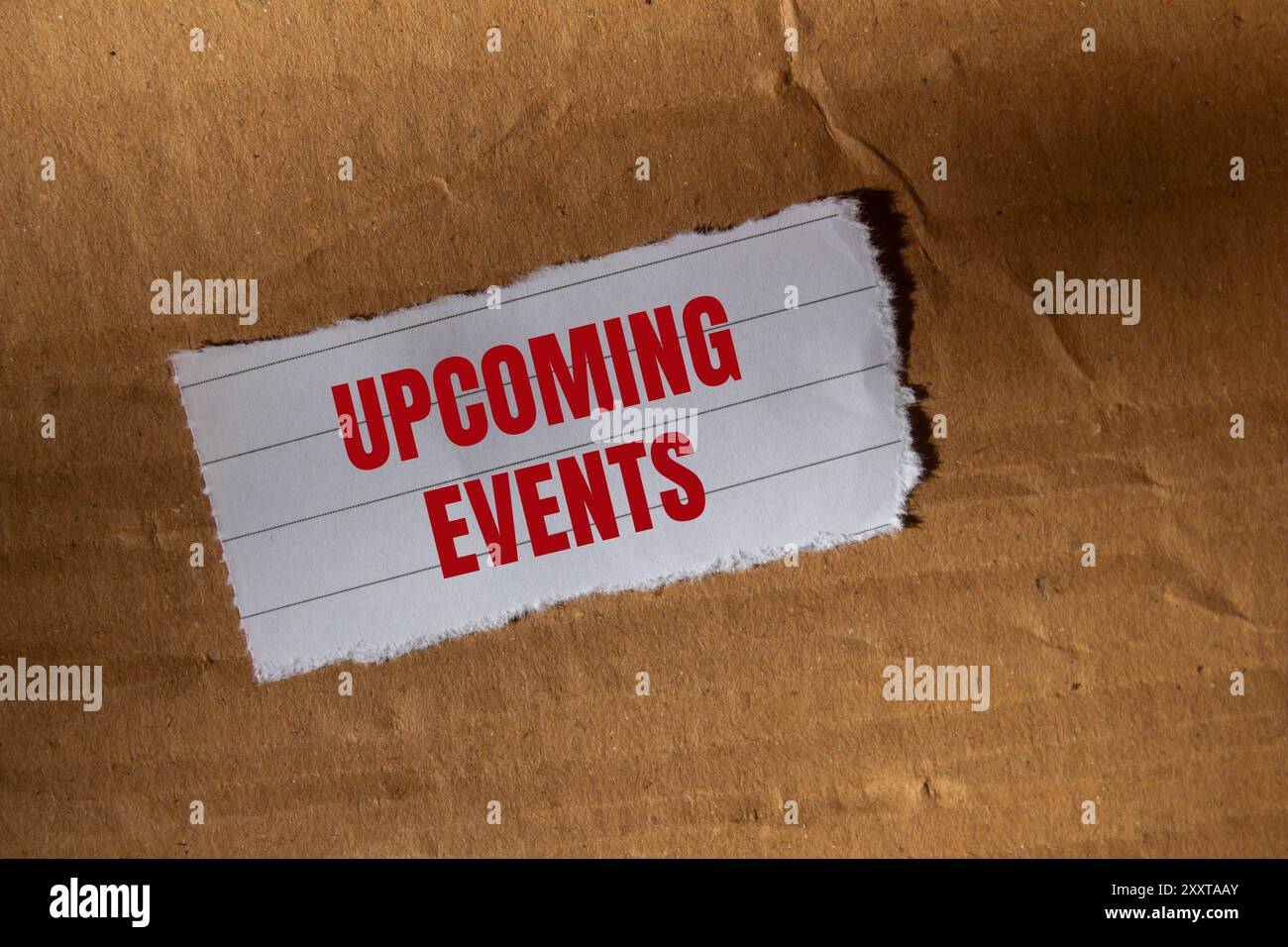 Upcoming events words written on ripped white paper piece with cardboard background. Conceptual ...