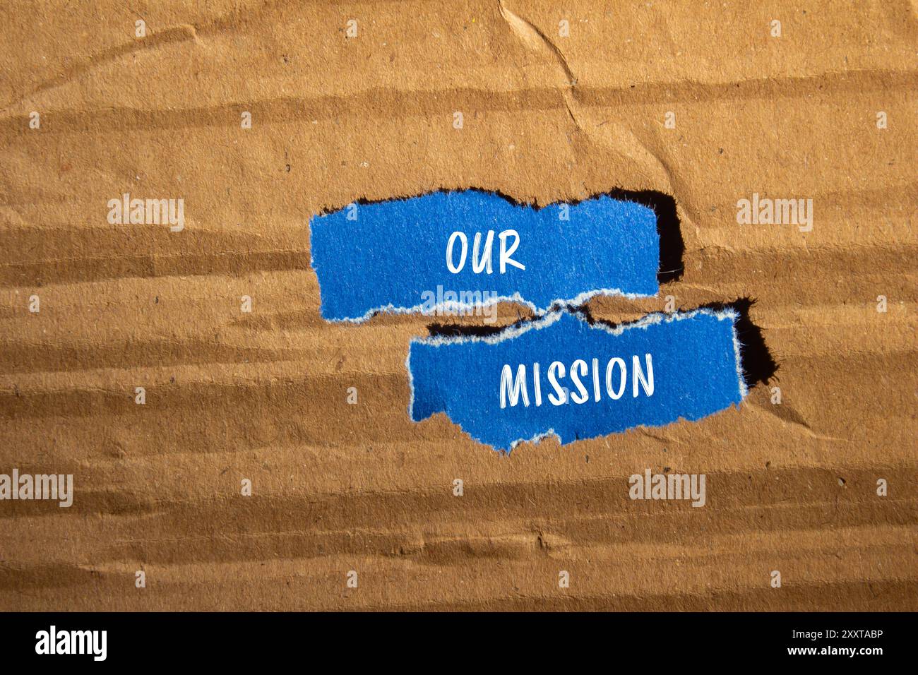 Our mission message written on ripped blue paper pieces with cardboard background. Conceptual ...