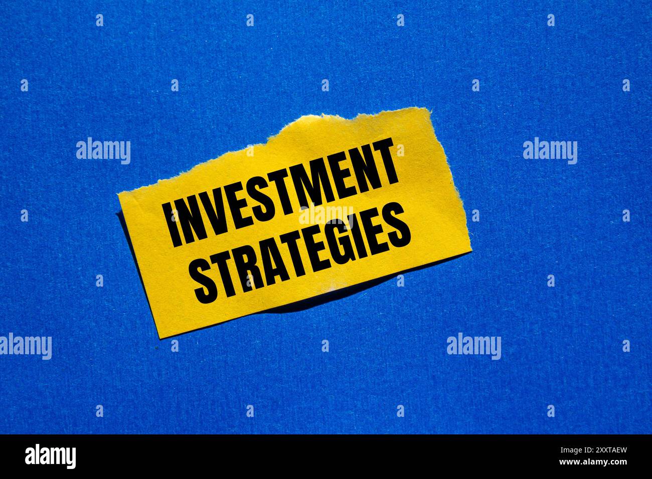 Investment strategies message written on ripped torn yellow paper piece with blue background ...