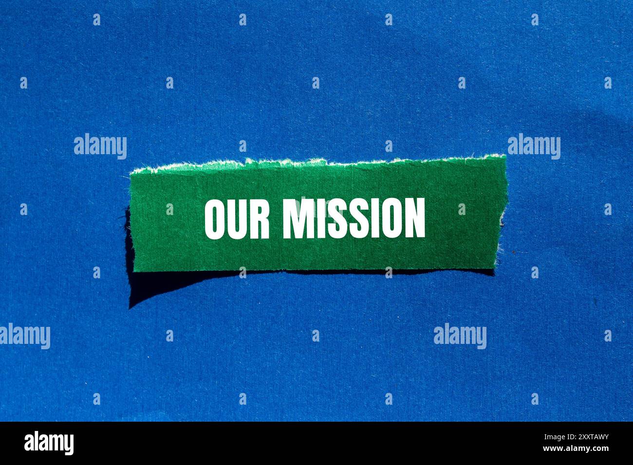 Our mission message written on ripped torn green paper piece on blue background. Conceptual our ...
