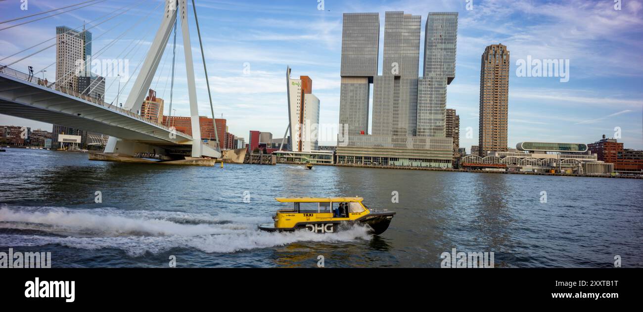 Wave creating water taxi passing urban skyline with Erasmus bridge and ...