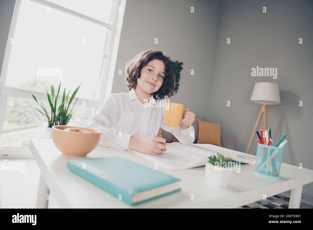 Photo of charming clever small boy schoolkid doing hometask eating snack room interior indoors ...
