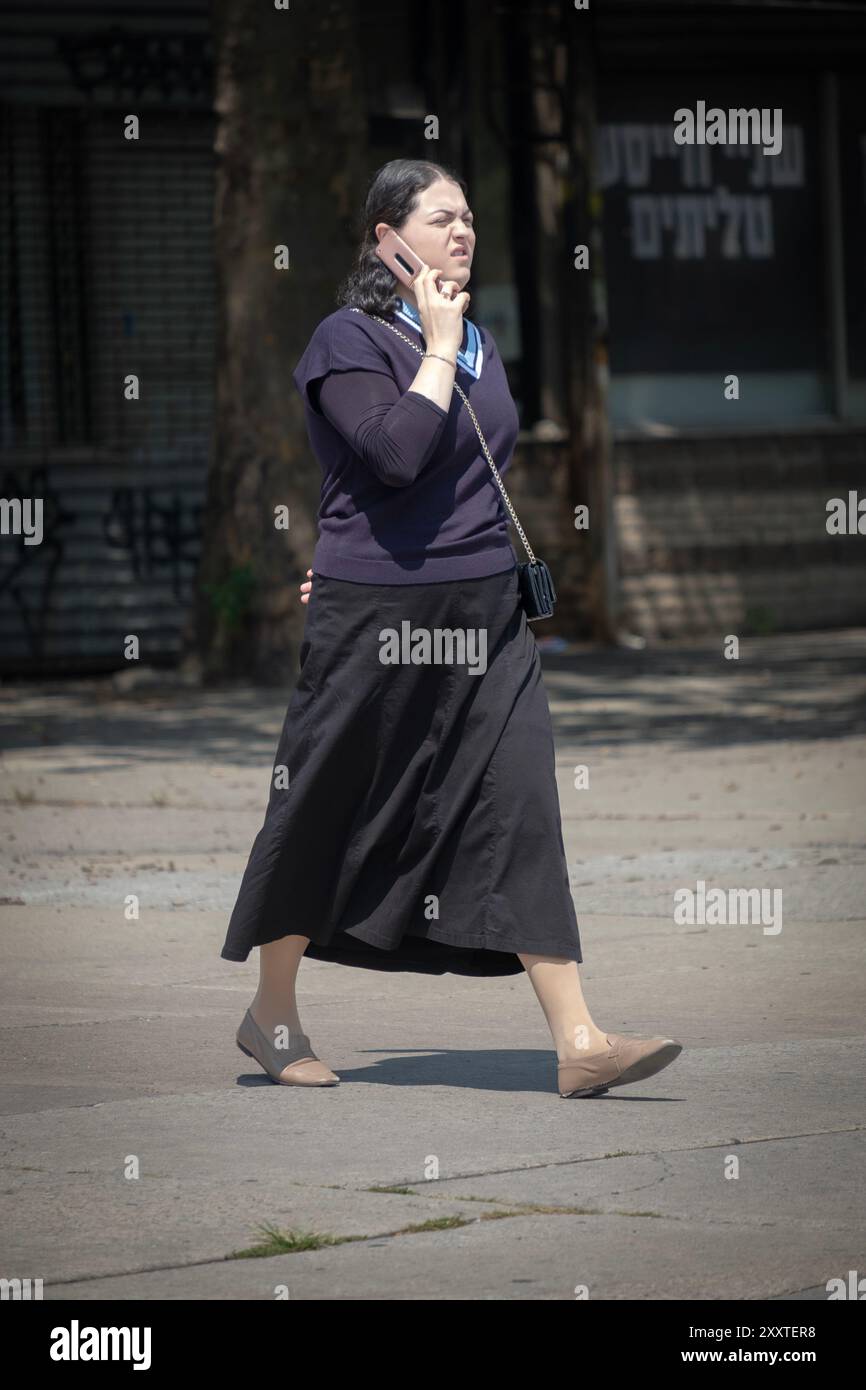 An orthodox Jewish woman walks on Lee Avenue while speaking on her flip ...