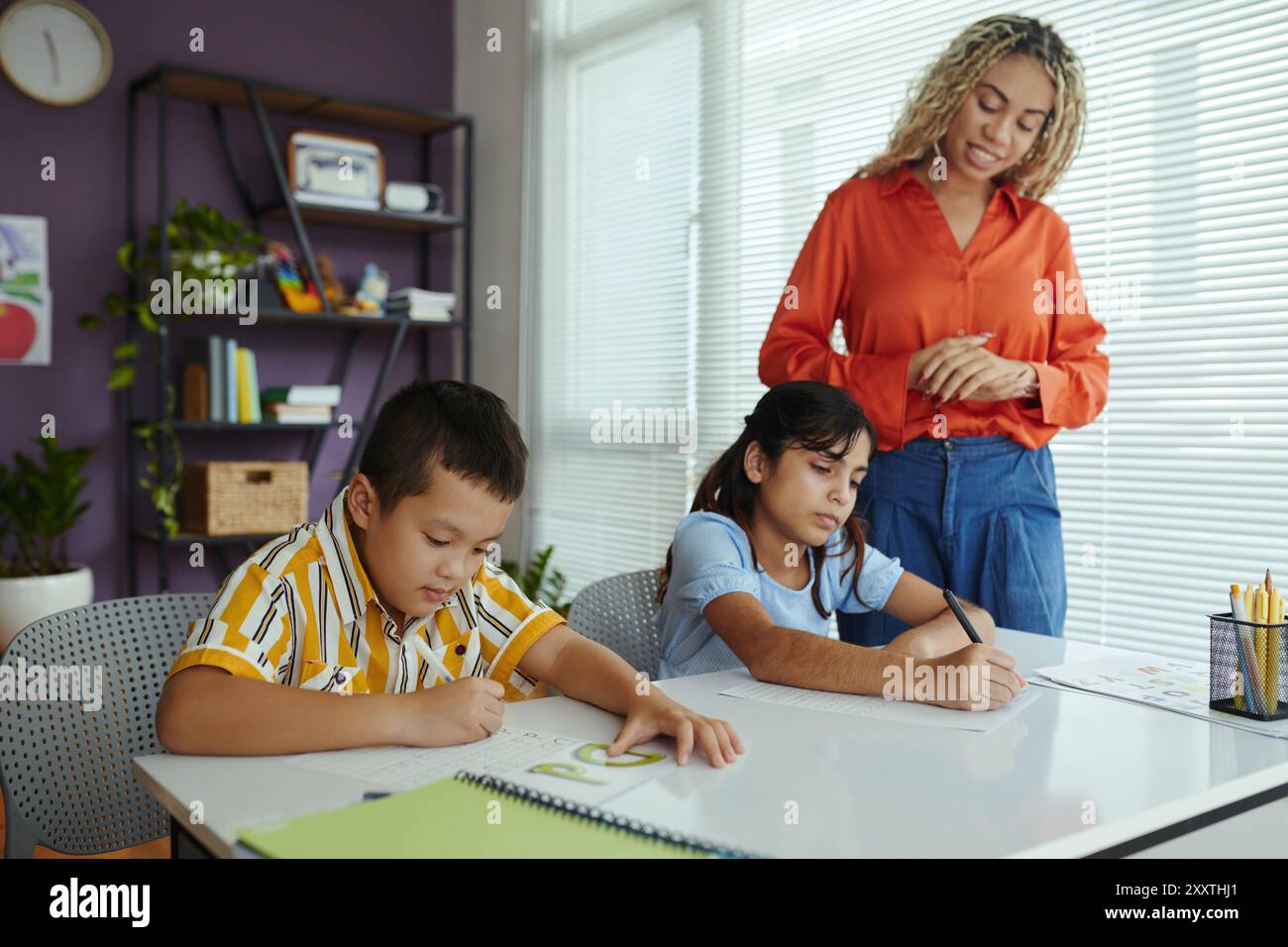 Children Writing in Classroom with Caring Teacher Watching Stock Photo ...