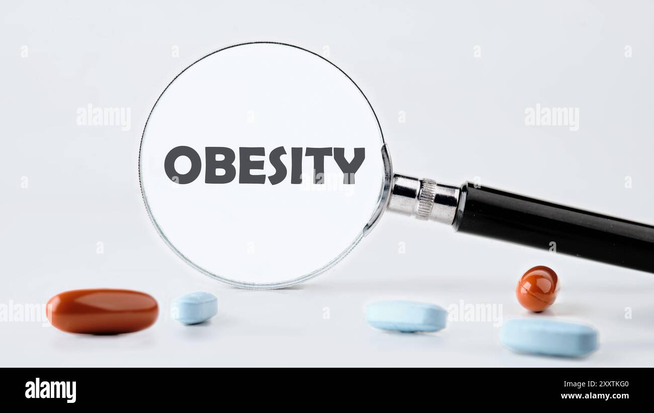 OBESITY word written through a magnifying glass on a gray background in ...