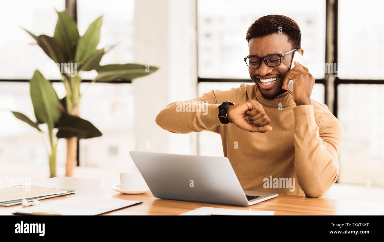 Happy black guy looking at watch talking on phone Stock Photo - Alamy