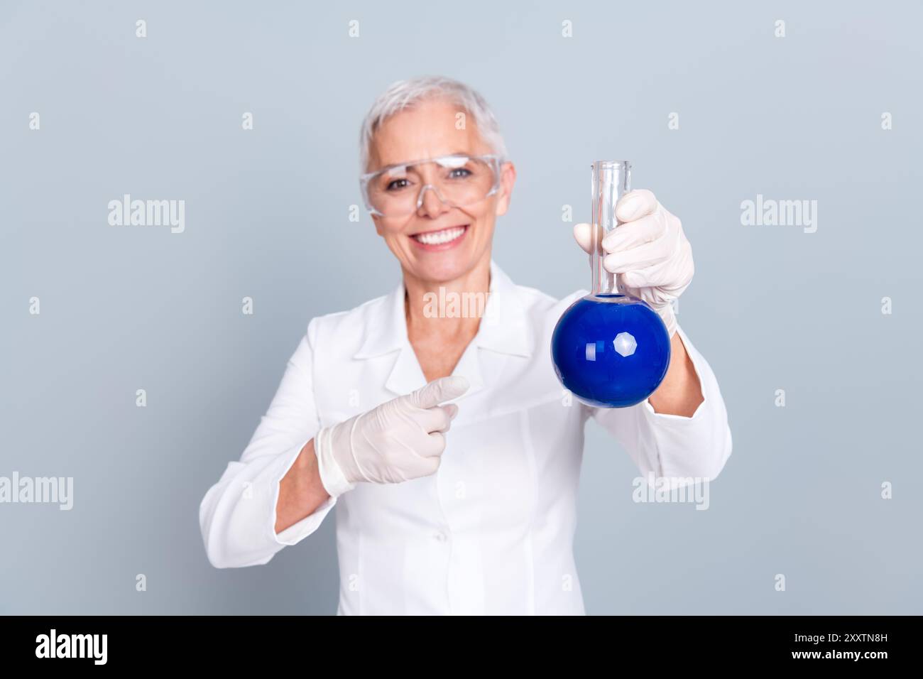 Photo of smiling old woman scientist point flask liquid beaker isolated ...