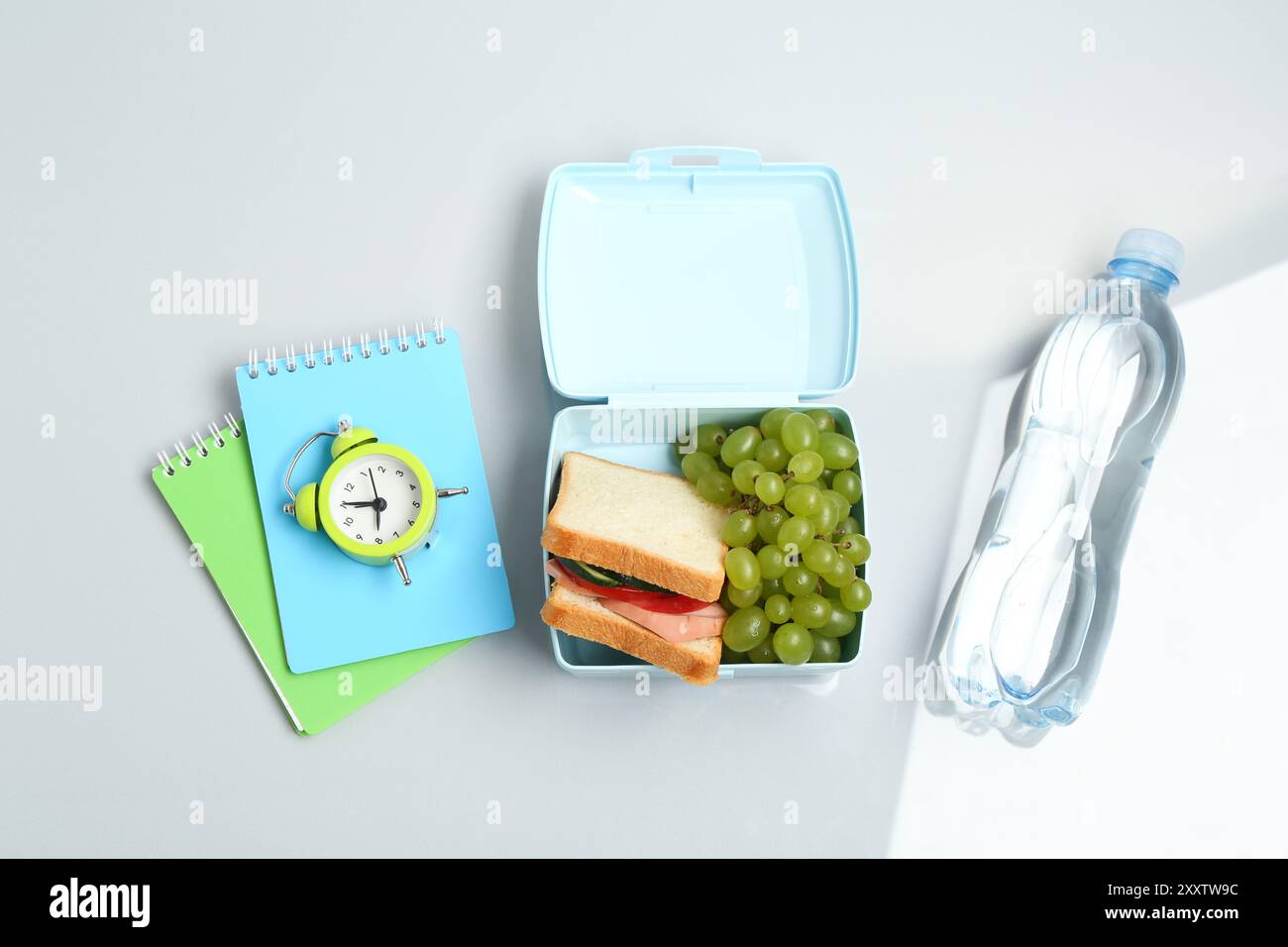 Lunch box with snacks, bottle of water, alarm clock and stationery on ...
