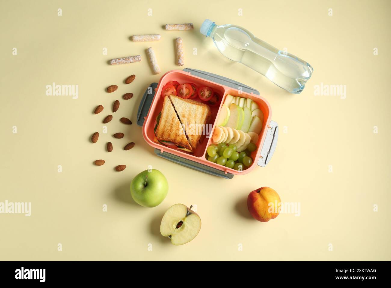 Lunch box with snacks and bottle of water on yellow table, flat lay ...