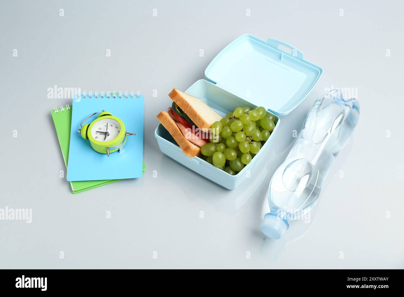 Lunch box with snacks, bottle of water, alarm clock and stationery on ...