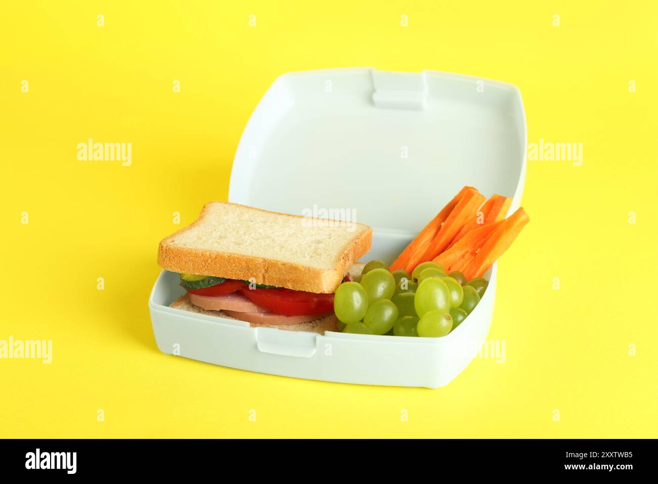 Lunch box with sandwich, carrot and grape on yellow background Stock ...