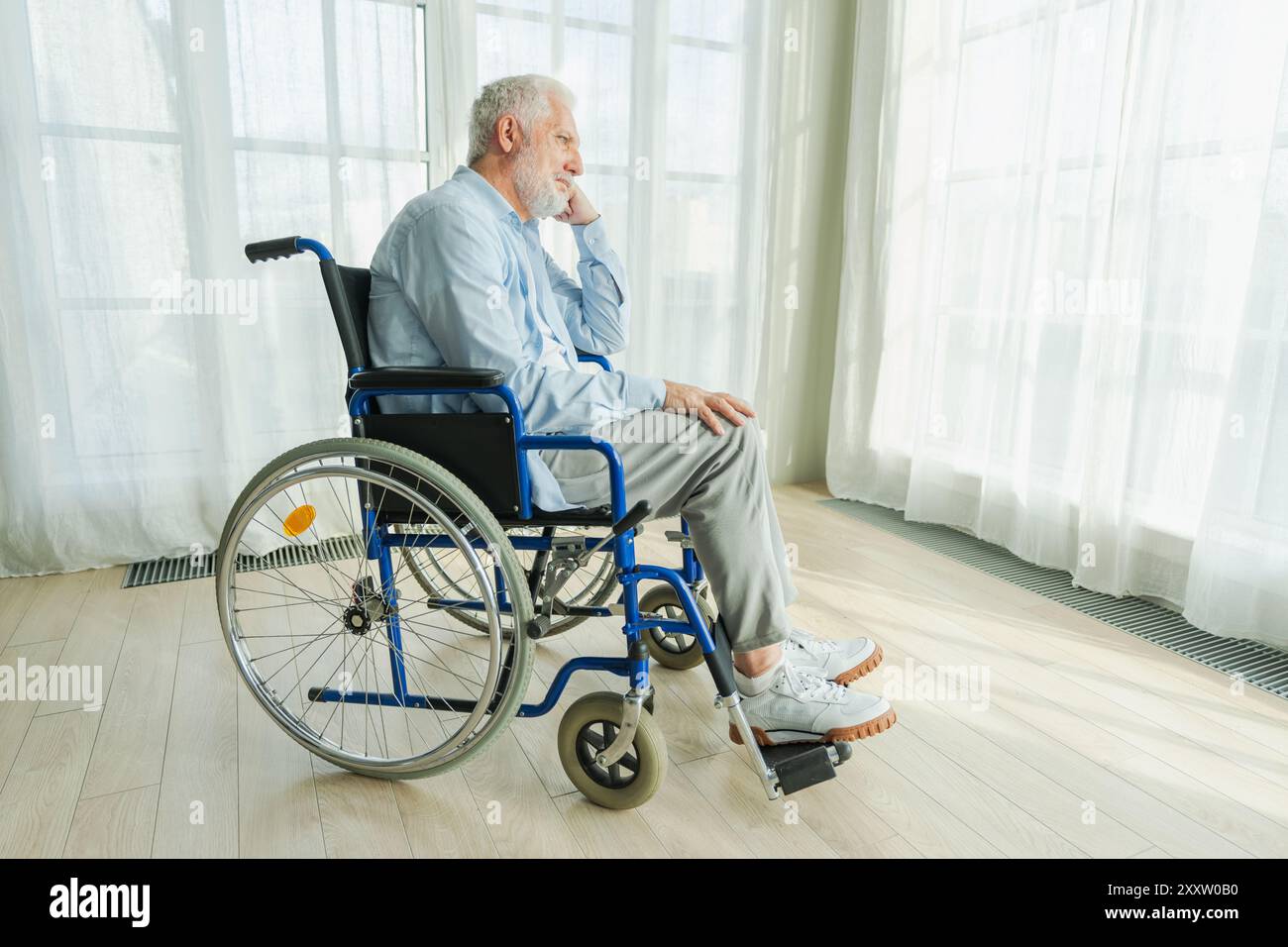 Sad senior man sitting in wheelchair looking out window in retirement ...