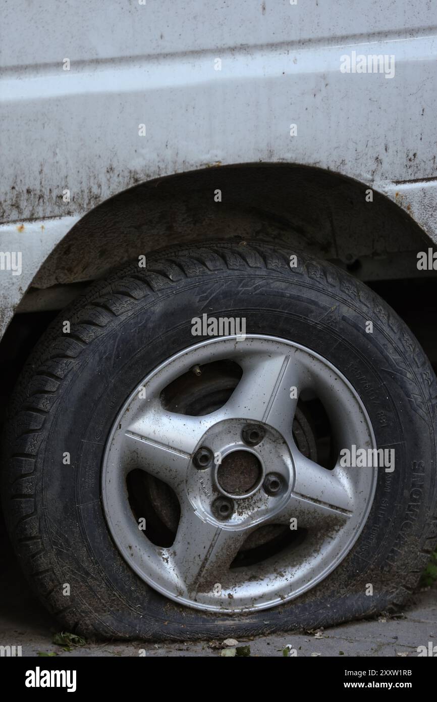 Dirty car wheel with a flat tire, showing signs of disuse. Vertical ...