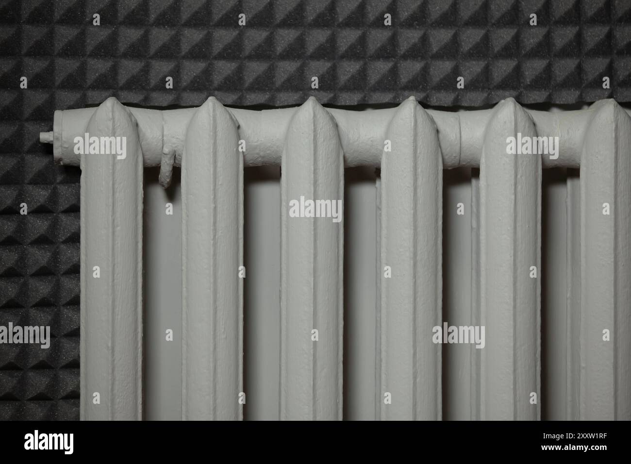 White radiator pipes set against a textured black wall, highlighting ...