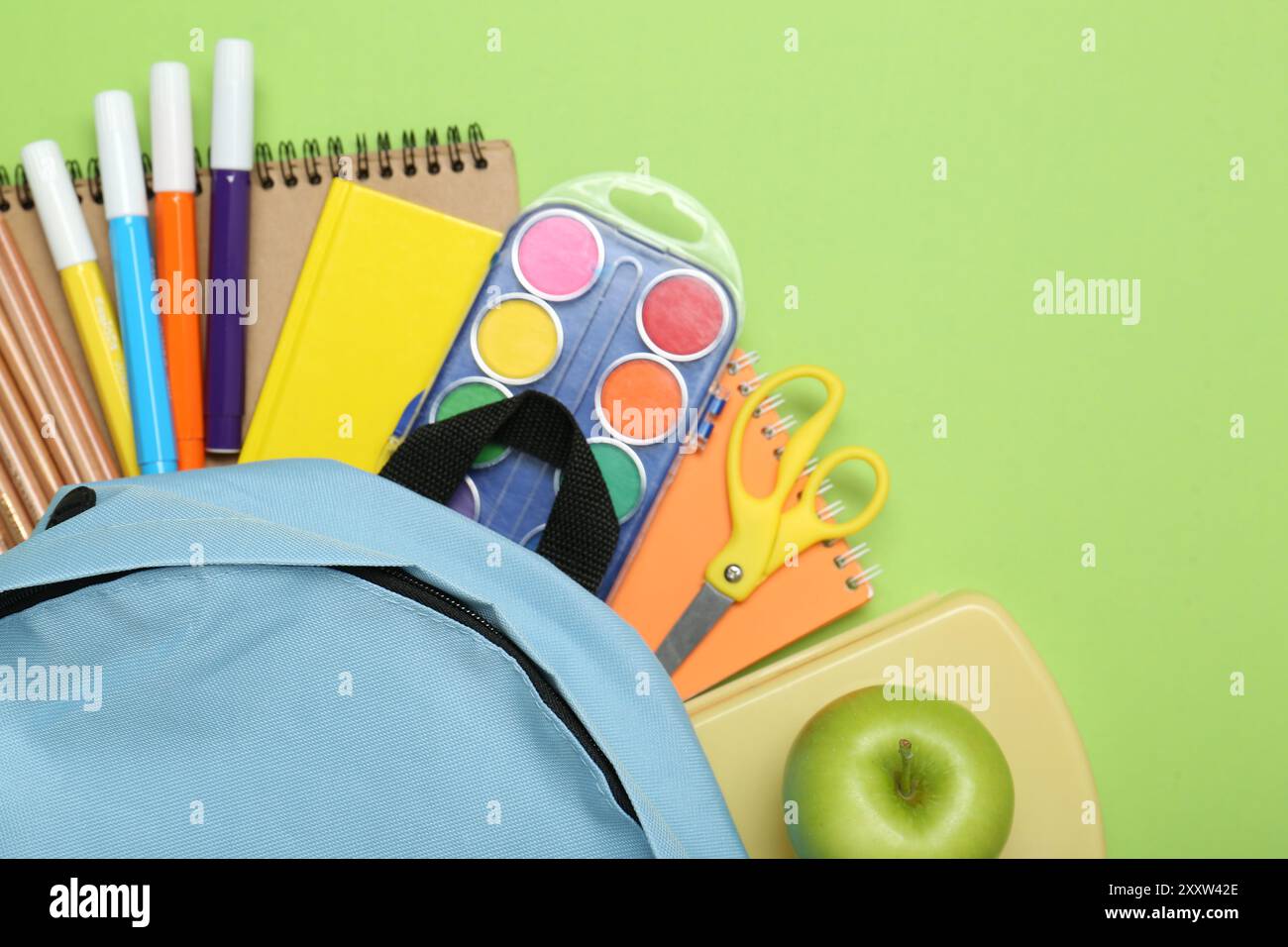Light blue school backpack with stationery on green background, top ...