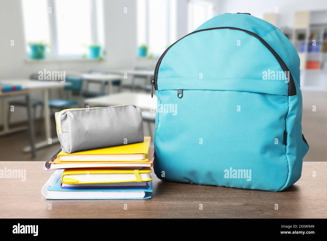 Light blue backpack with stationery on school desk in classroom. Space ...