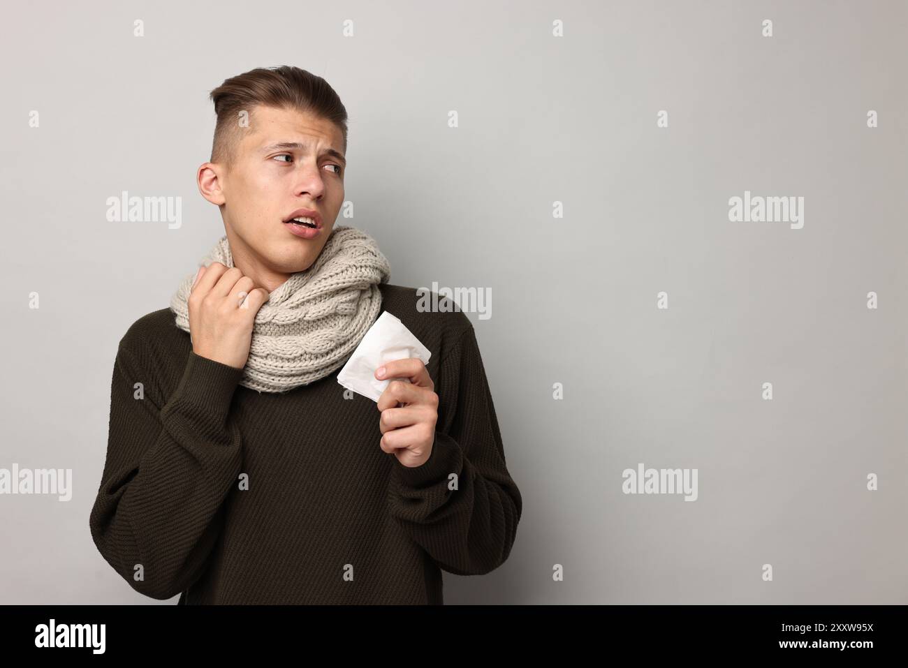 Sick man with tissue suffering from cold symptoms on light grey ...
