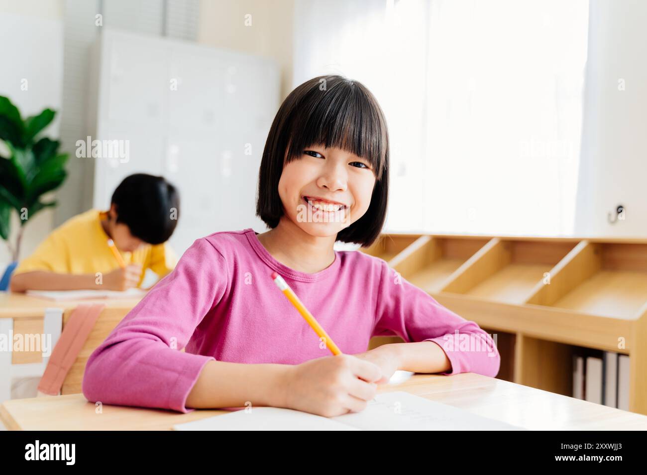 Enthusiastic young learner engages with camera during writing task ...