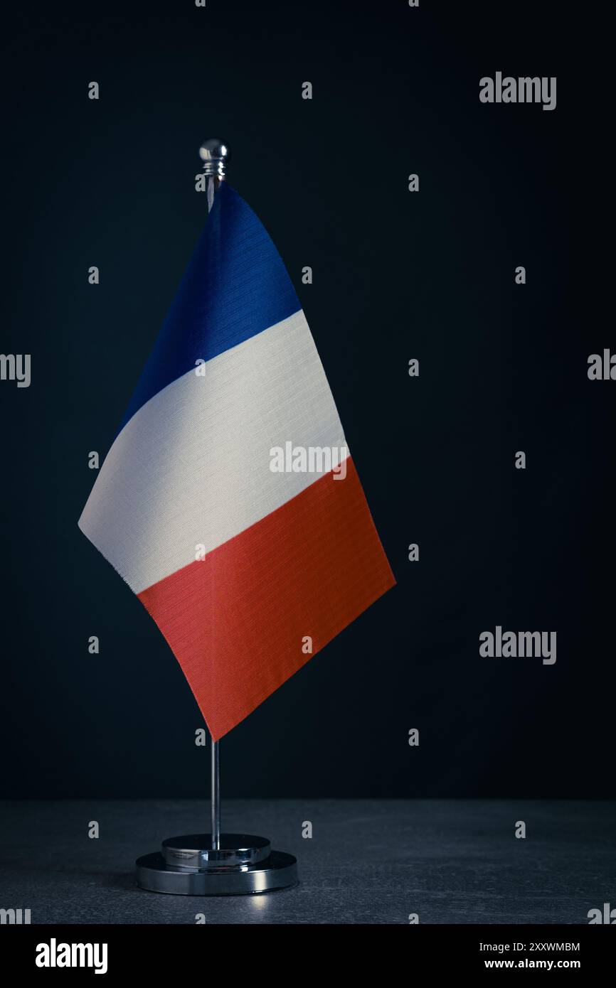 Flag France on metal flagpole, illuminated one side, dark background ...