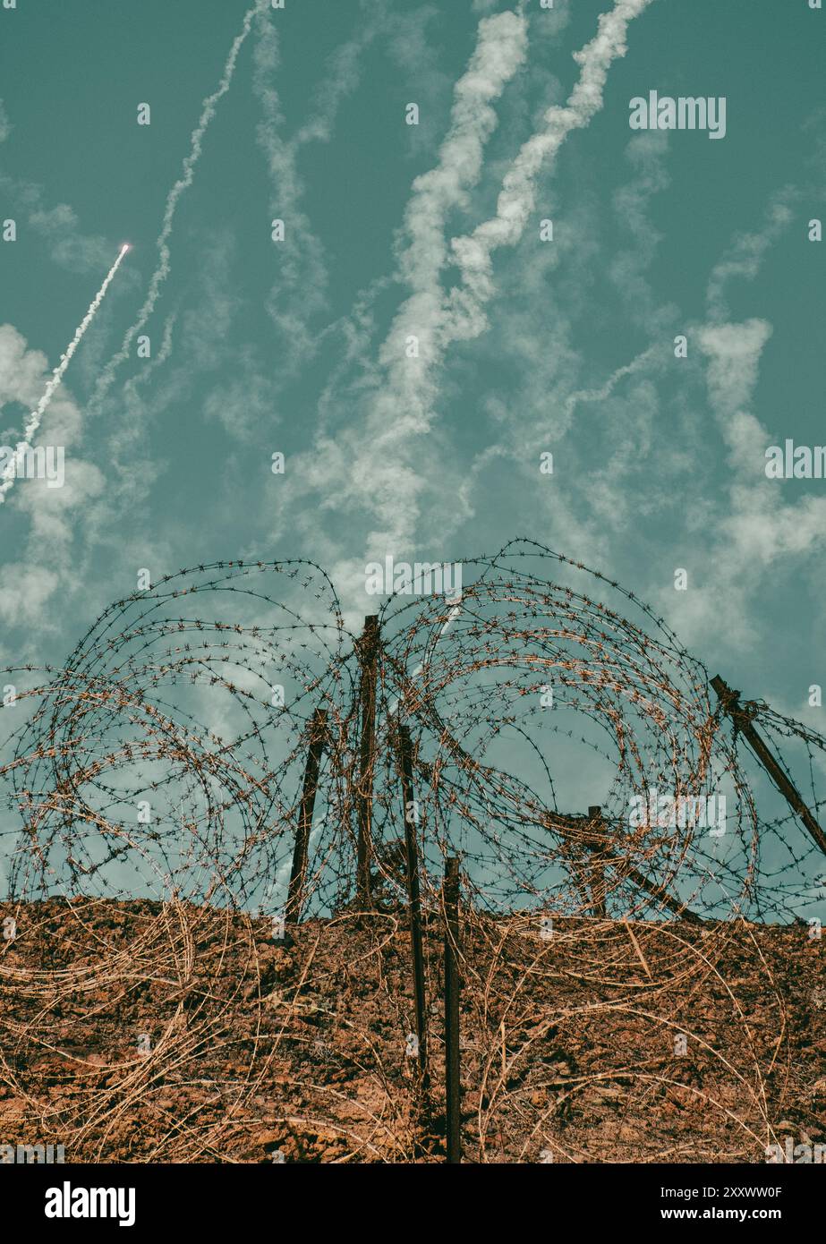 Rolls of barbed wire with rocket fire smoke trails in sky. Concept: war ...