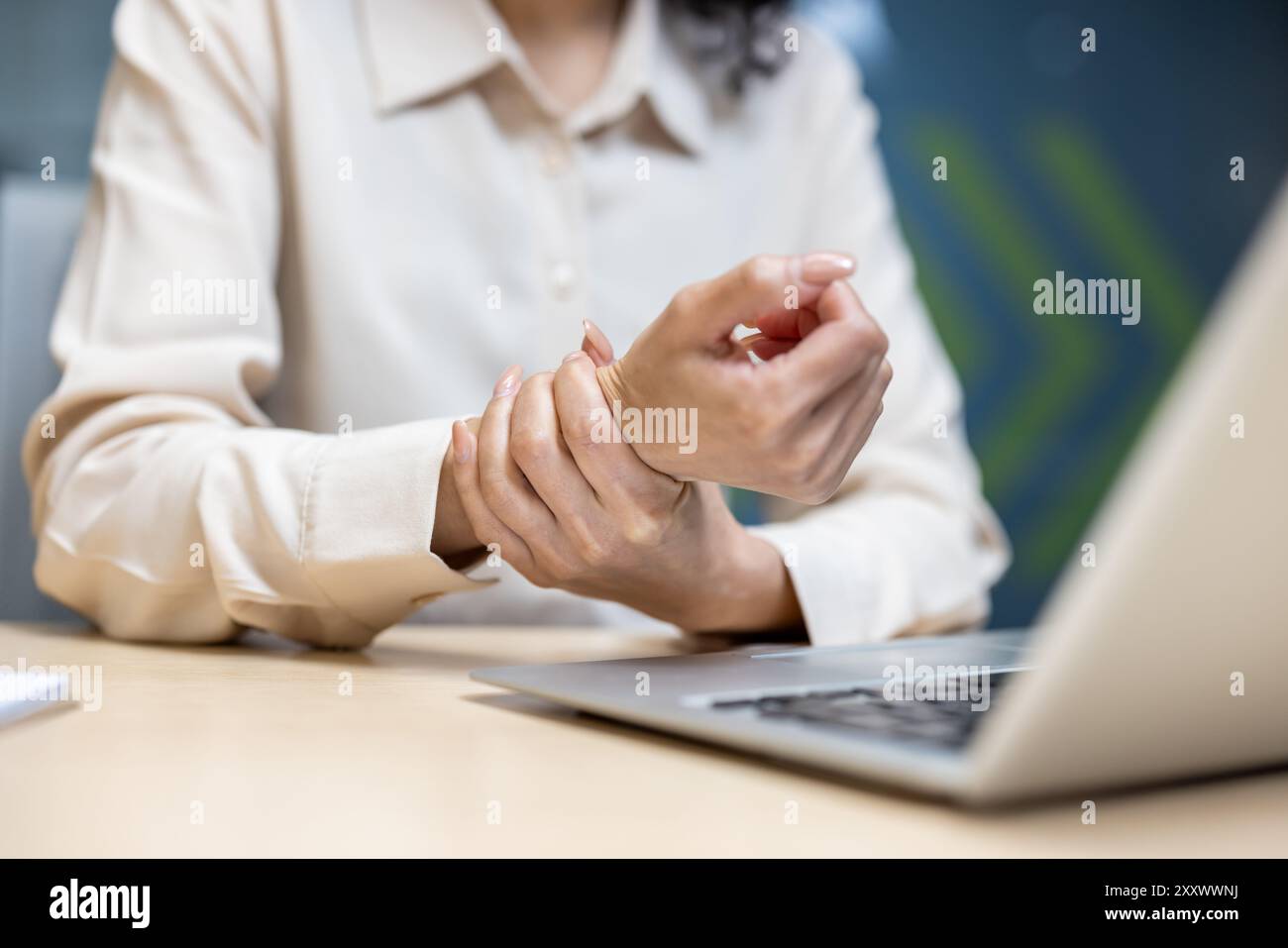 Office worker holds wrist in pain while working on laptop, showing ...