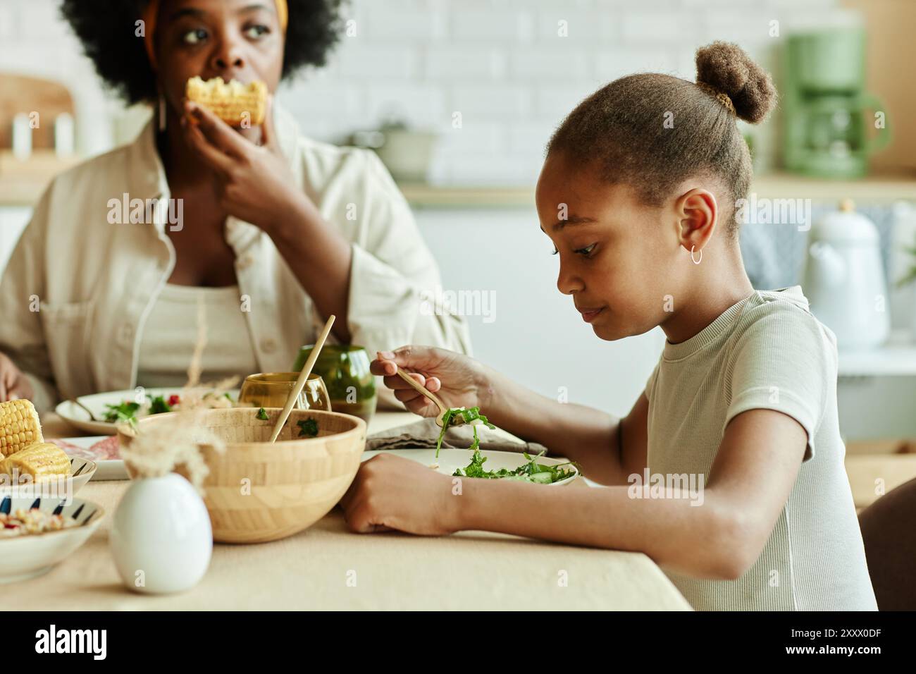Side view of little African American girl eating balanced meal during family dinner at kitchen ...