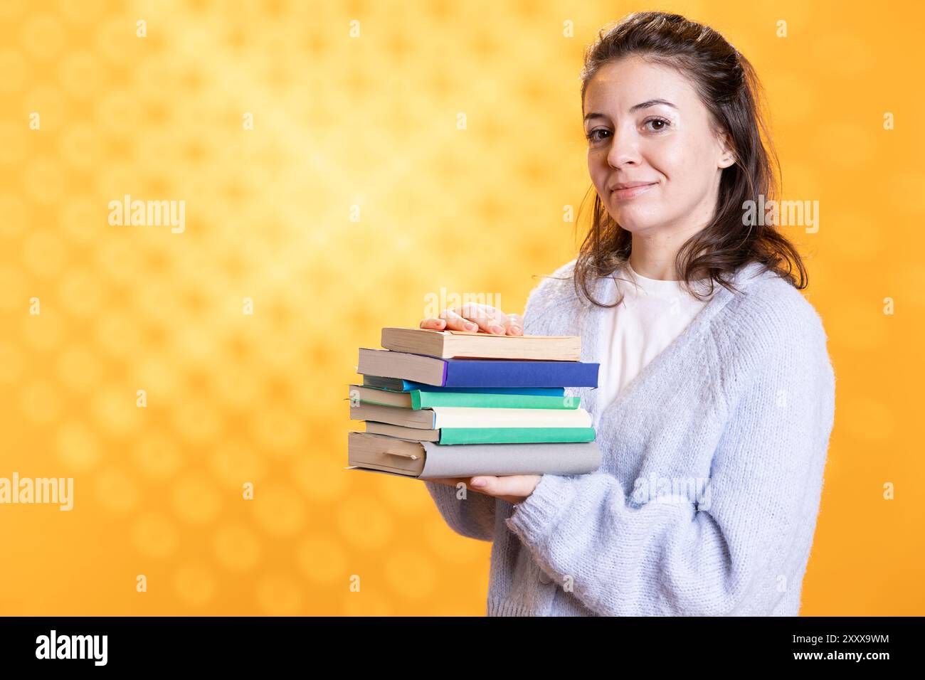 Portrait of merry woman smiling while holding pile of books, enjoying ...