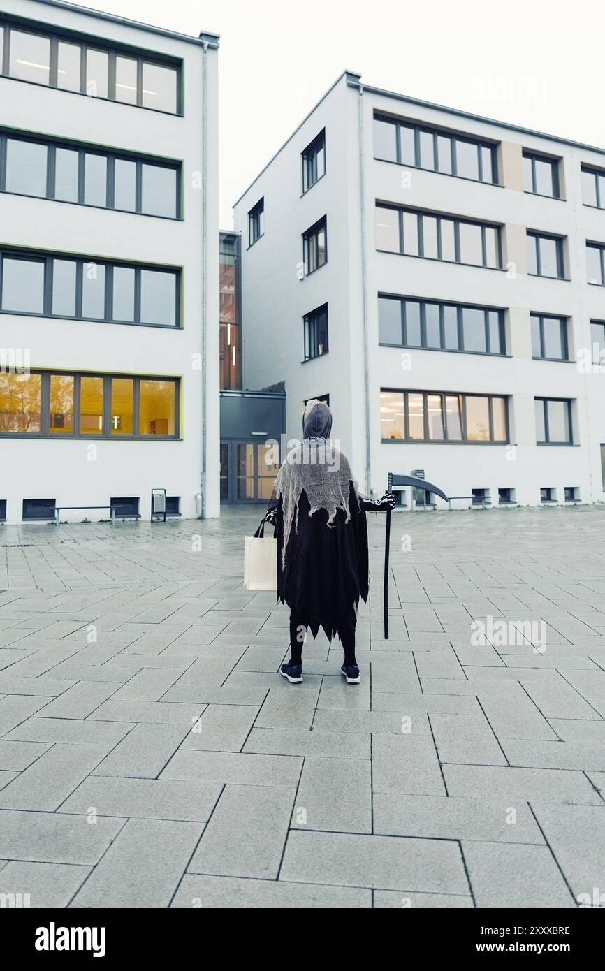 Back view of kid in grim reaper Halloween costume with scythe and bag ...