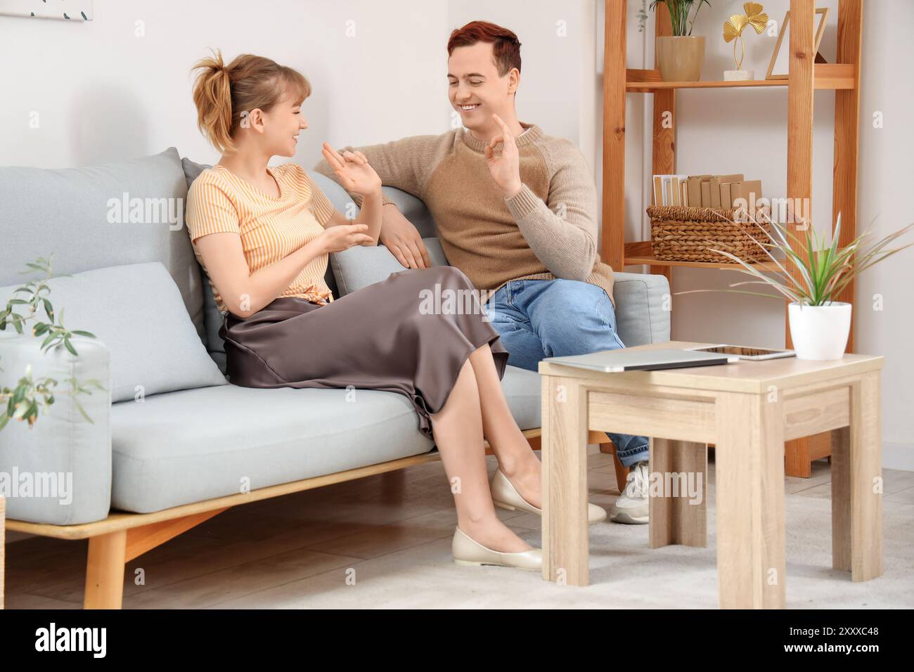 Young deaf mute couple using sign language on sofa at home Stock Photo ...