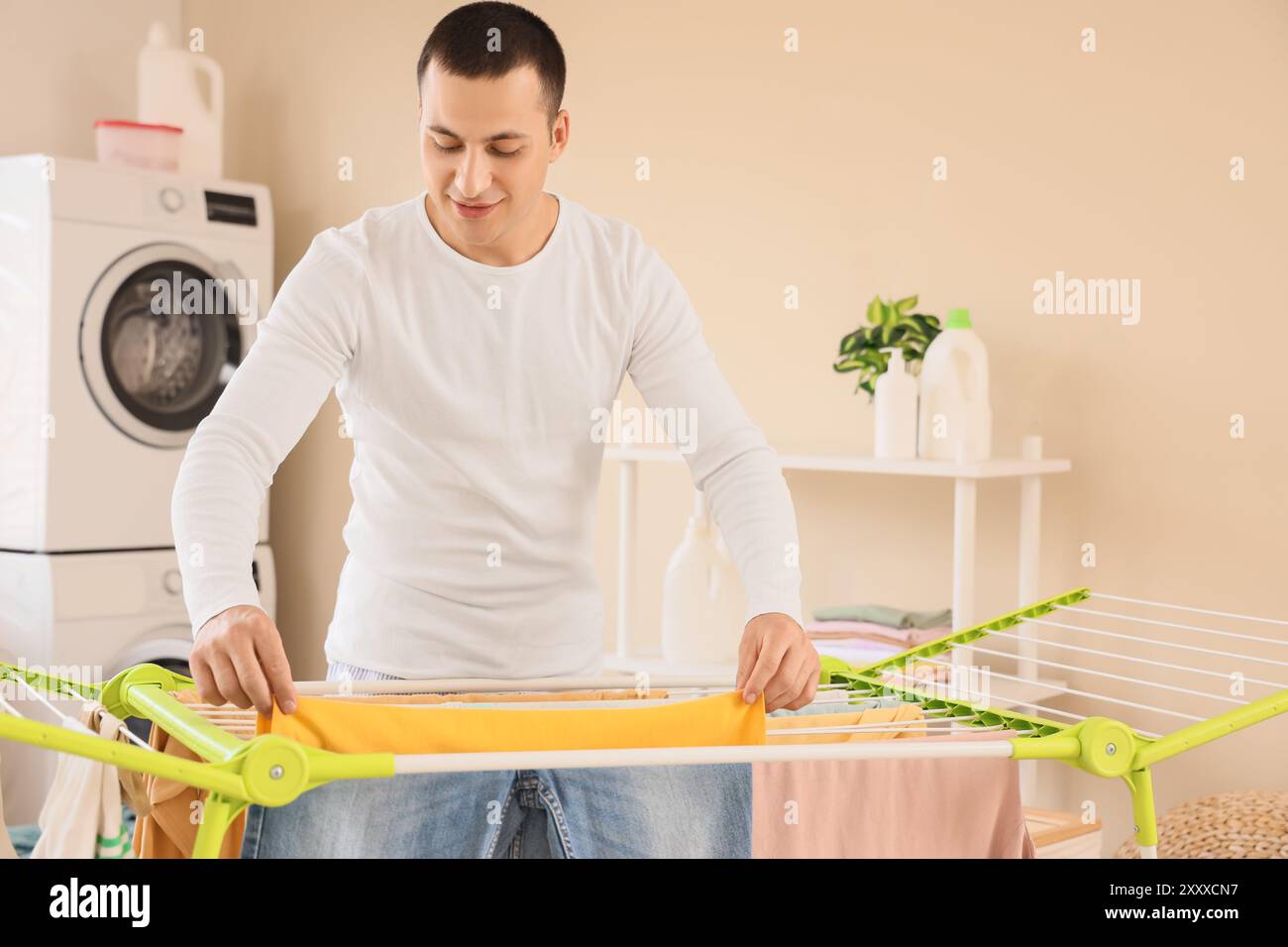 Young man hanging clean clothes on dryer in laundry room Stock Photo ...