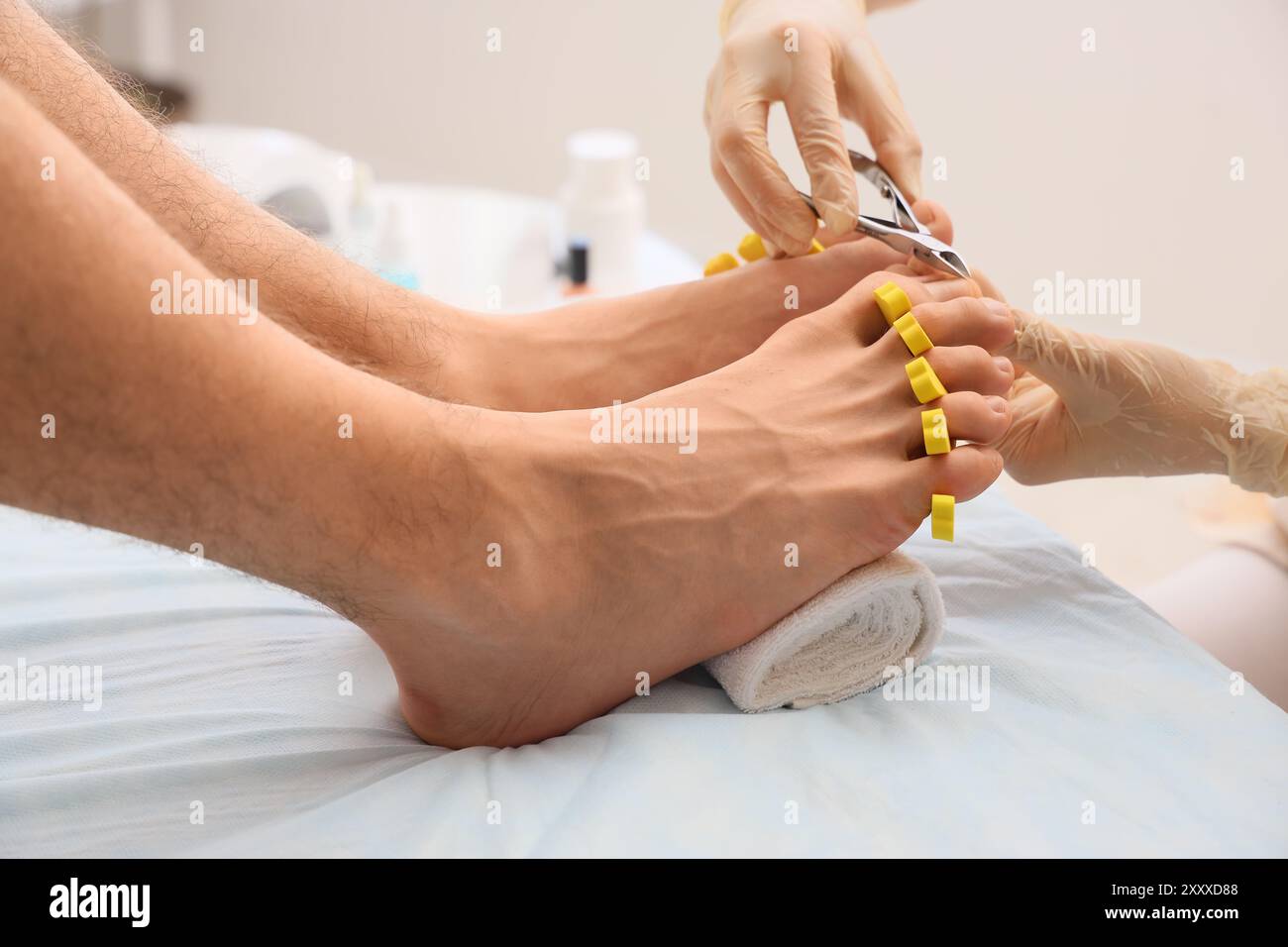 Beautician cutting cuticle off feet of young man with toe separator on ...
