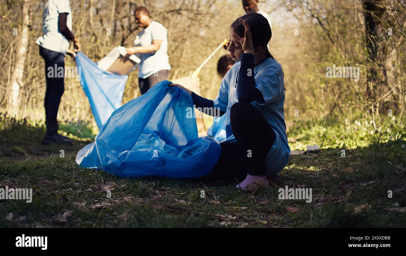 Tired little girl collecting trash and plastic bottles from the forest ...