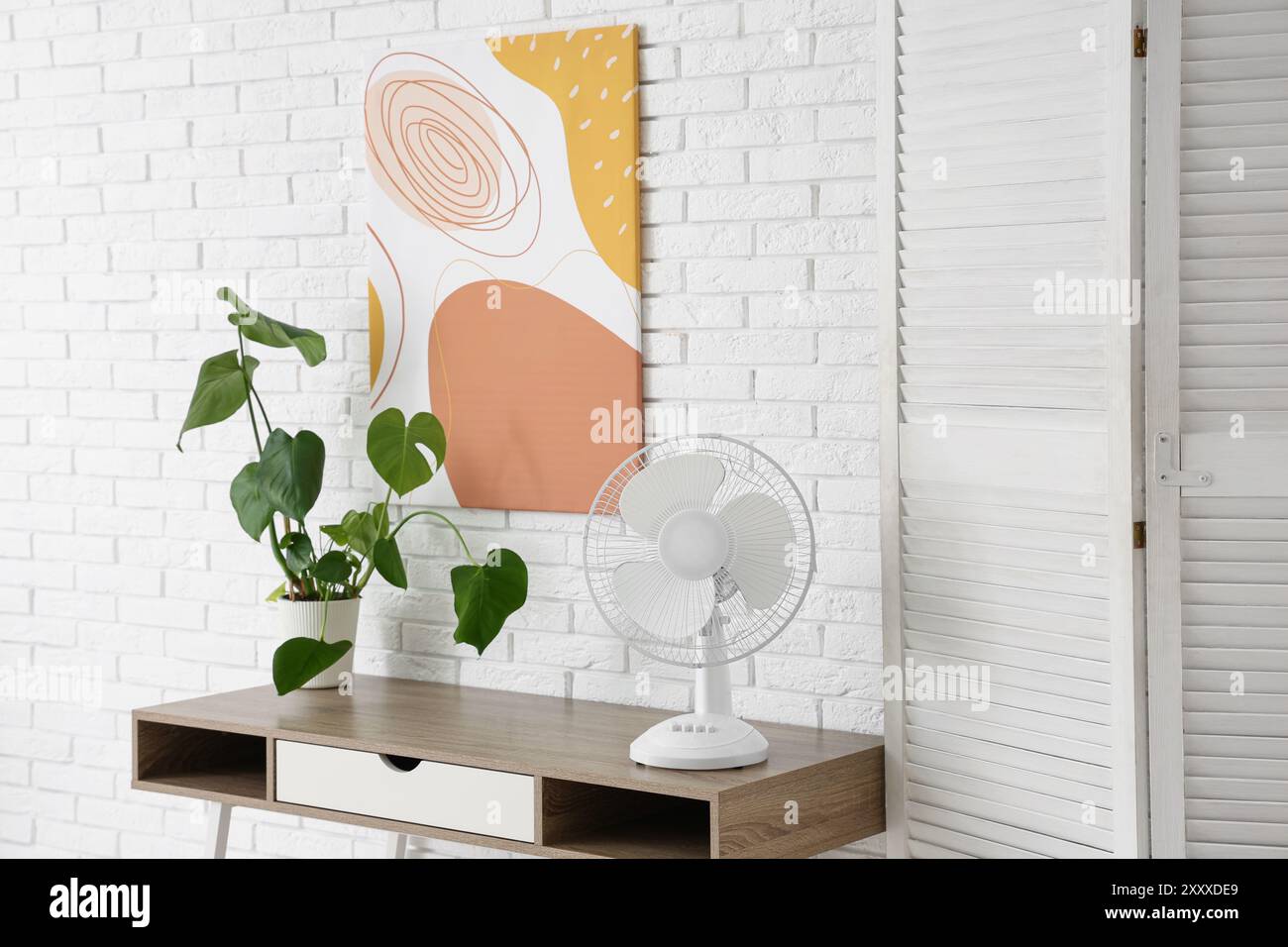 Modern electric fan on table with houseplant near picture and white ...