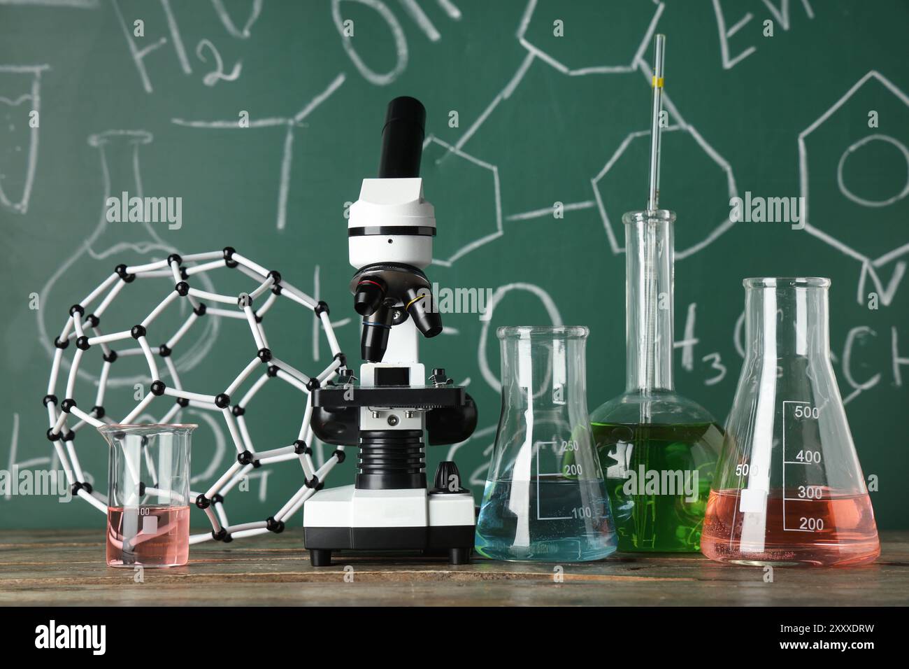 Modern microscope, molecular model and flasks on wooden table near ...