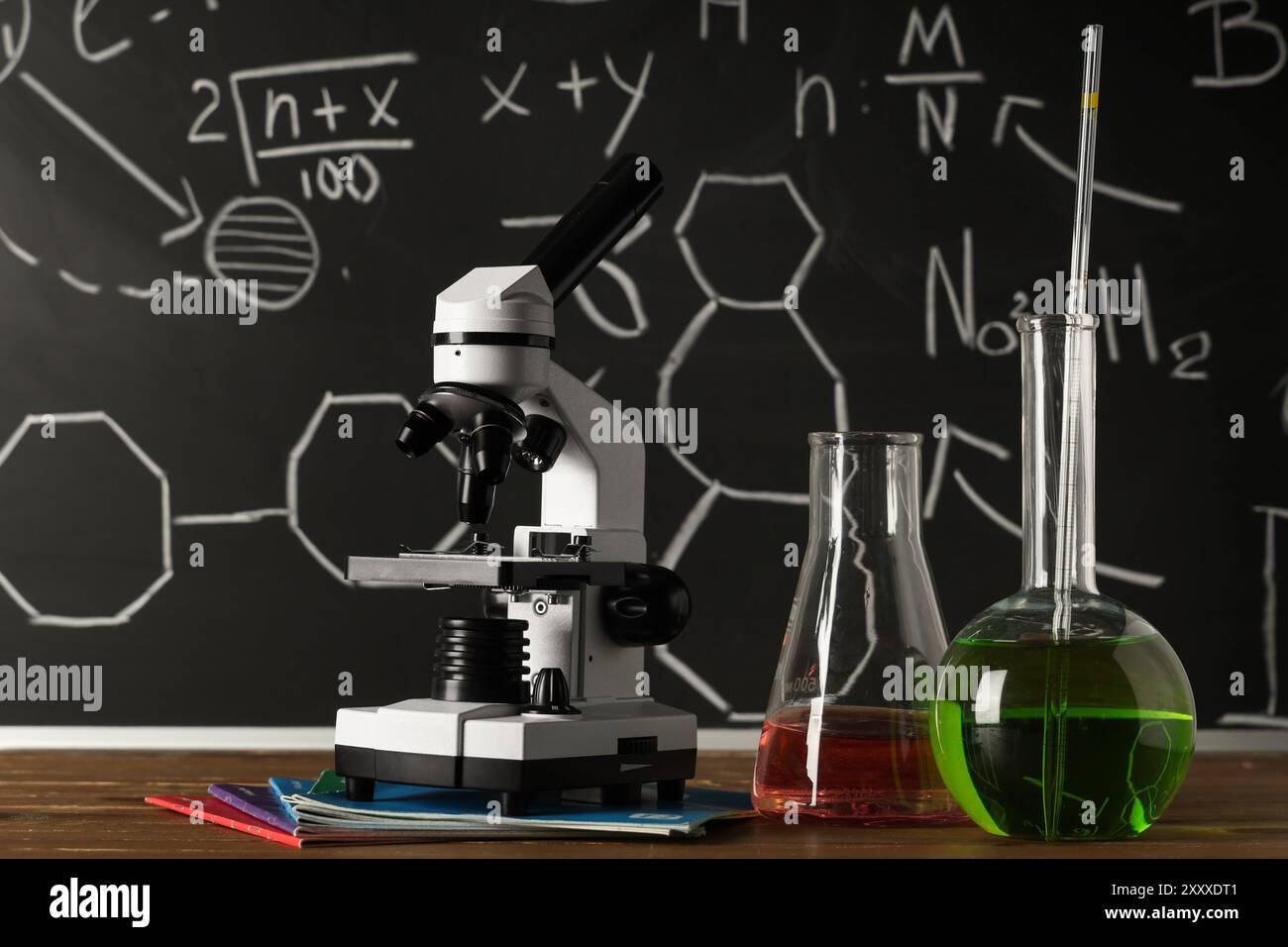 Modern microscope and flasks on wooden table near chalkboard with ...