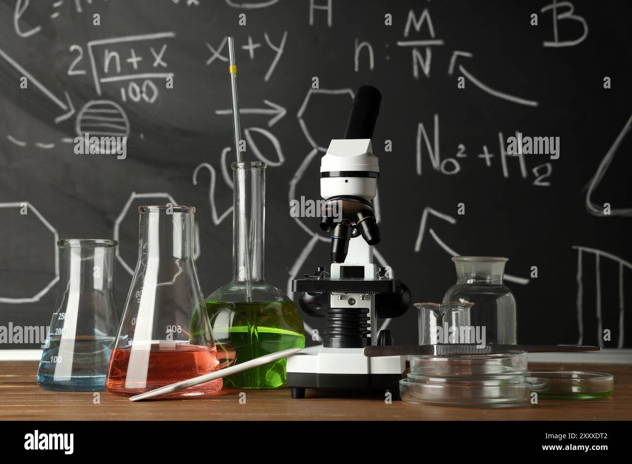 Modern microscope, petri dishes and flasks on wooden table near ...