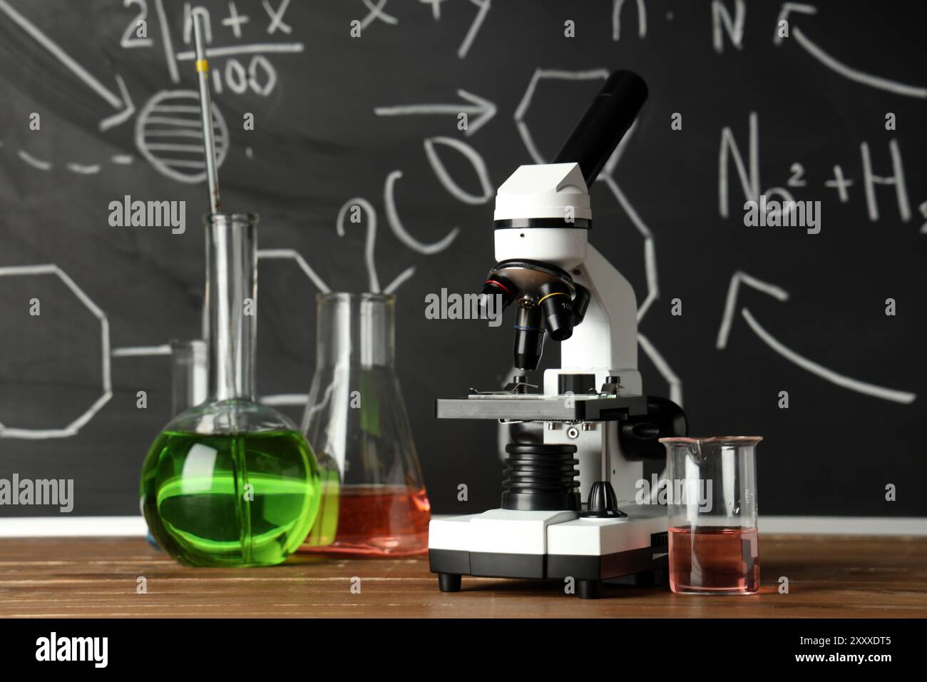 Modern microscope and flasks on wooden table near chalkboard with ...