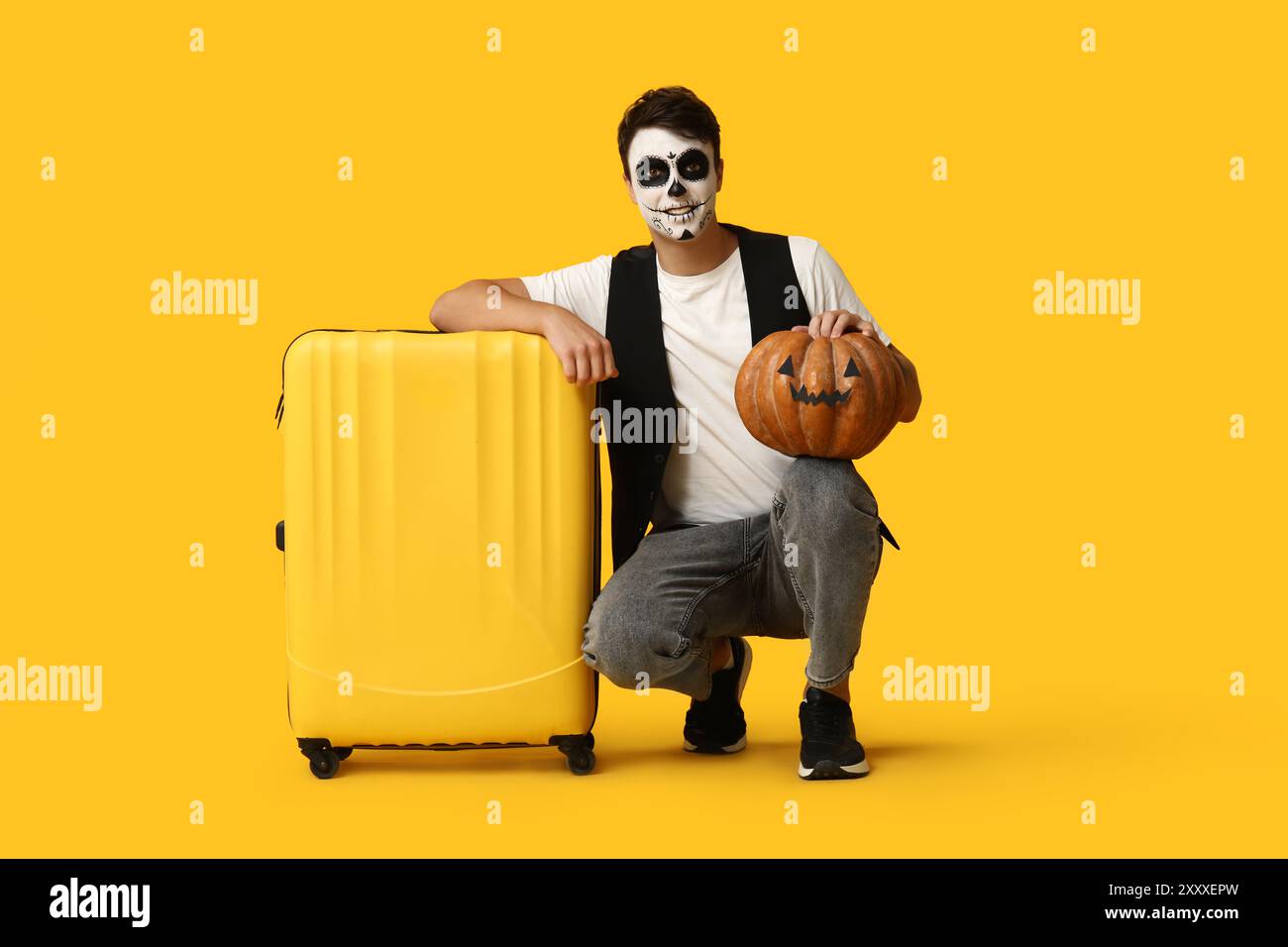 Male tourist dressed for Halloween with pumpkin and suitcase on yellow ...